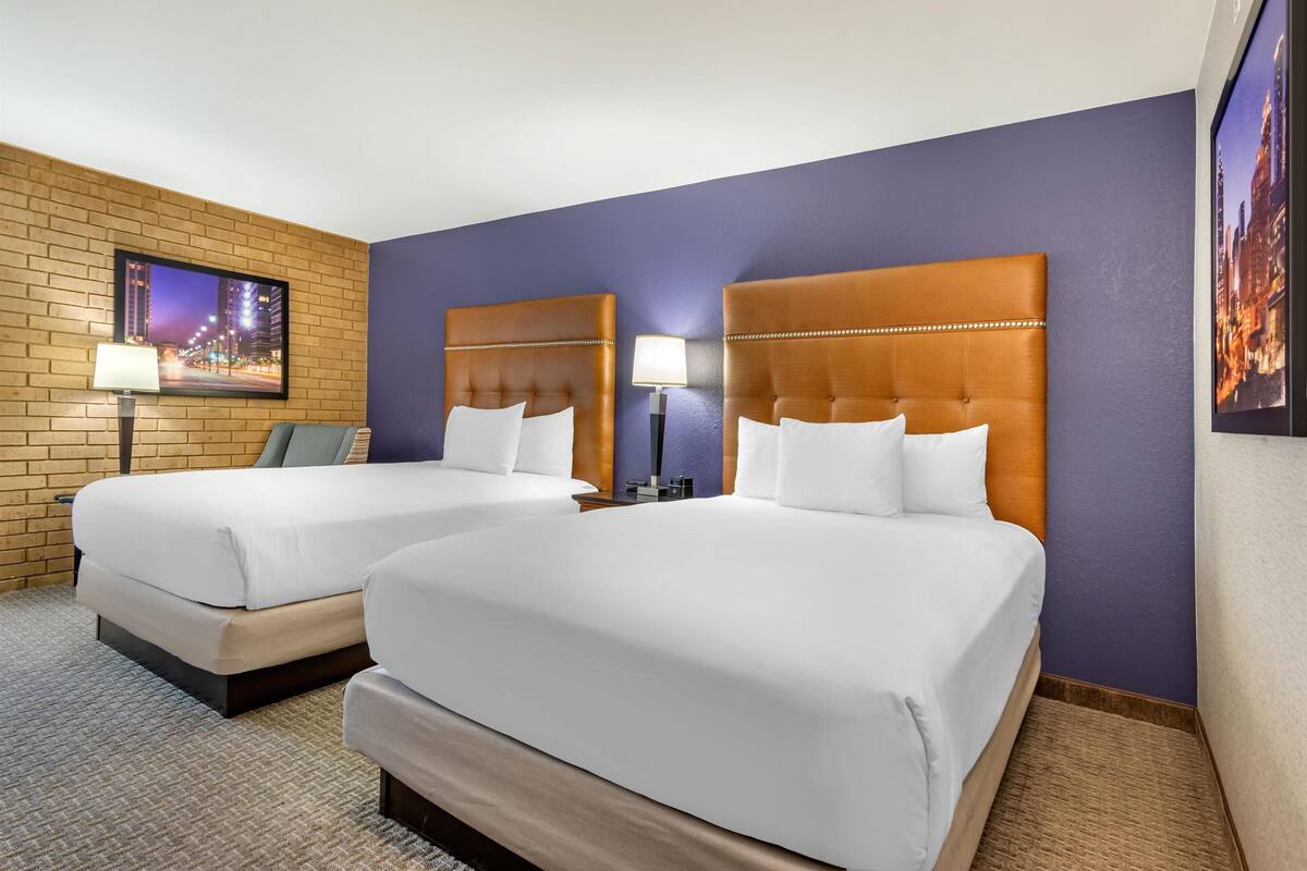 Quarto de hotel com duas camas, parede de tijolos e uma fotografia de paisagem urbana.