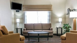 Uma sala de estar com sofá, duas poltronas, uma mesa de centro, televisão e uma janela com cortinas.