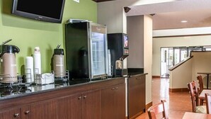 Cozinha compacta com geladeira, cafeteira e micro-ondas. Possui uma área de refeições com cadeiras de madeira e mesa.