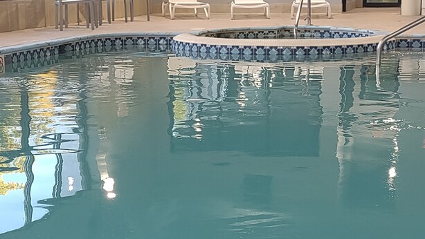 Piscina interna com água cristalina, rodeada por espreguiçadeiras e uma parede de vidro.