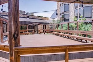 Um deck de madeira com bancos, rodeado por edifícios de tijolo e vegetação.
