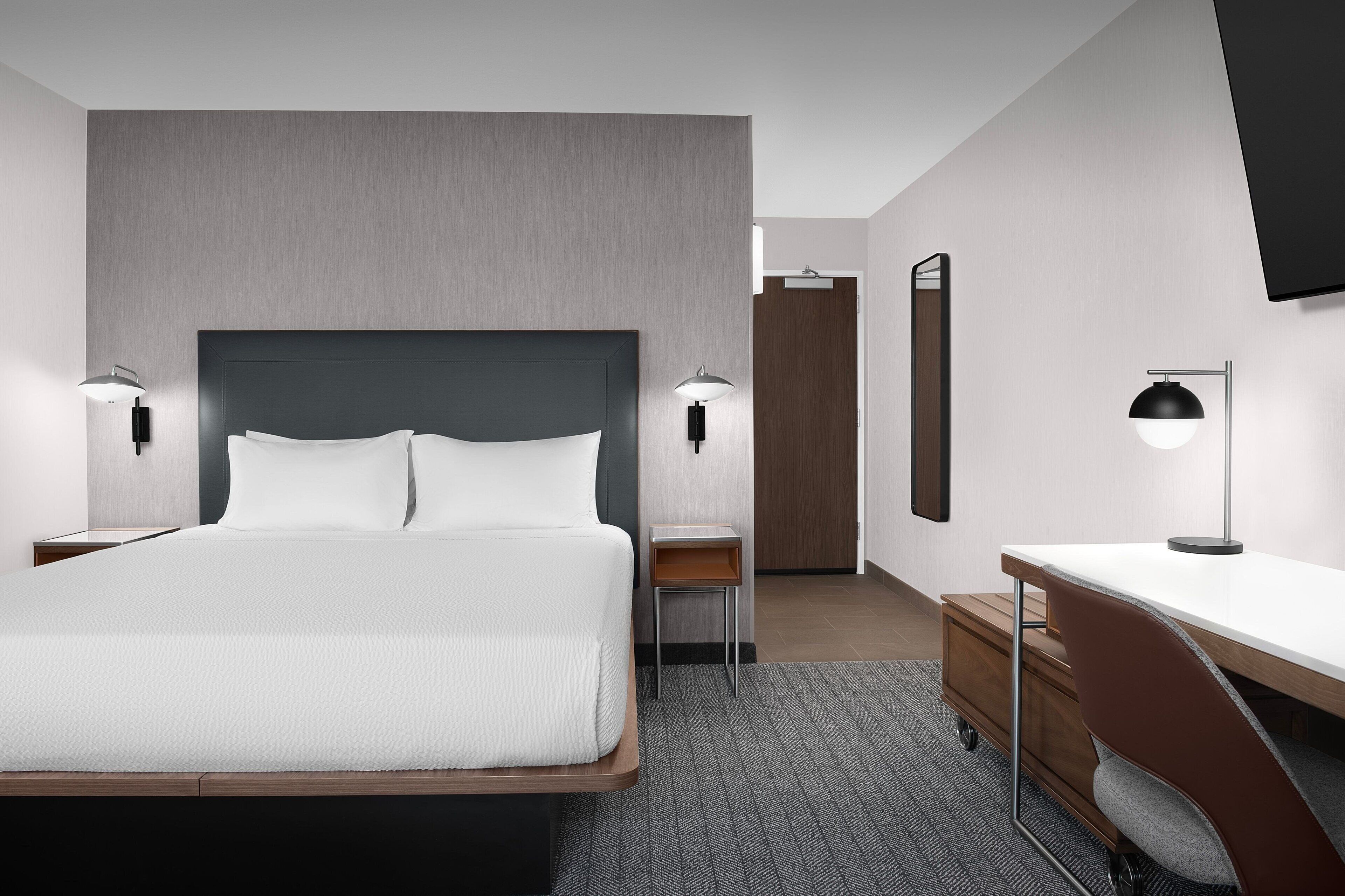 Quarto de hotel moderno com uma cama grande, uma escrivaninha e uma TV de tela plana na parede.