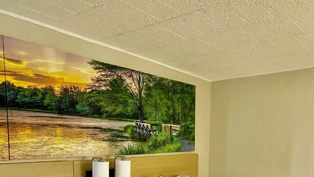 Quarto de hotel com duas camas, uma pintura de uma paisagem ao pôr do sol, uma mesa de cabeceira com abajur e um telefone.