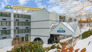 Um hotel Days Inn com design moderno, apresentando vários andares, janelas amplas e uma placa indicando comodidades como café da manhã gratuito, salas de banquetes e reuniões, internet de alta velocidade e piscina coberta e jacuzzi.