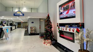 Um saguão de hotel com uma mesa de recepção, um pinheiro de Natal e uma televisão exibindo notícias.