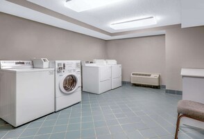 Uma lavanderia com máquina de lavar, secadora e cestos de roupa empilhados.