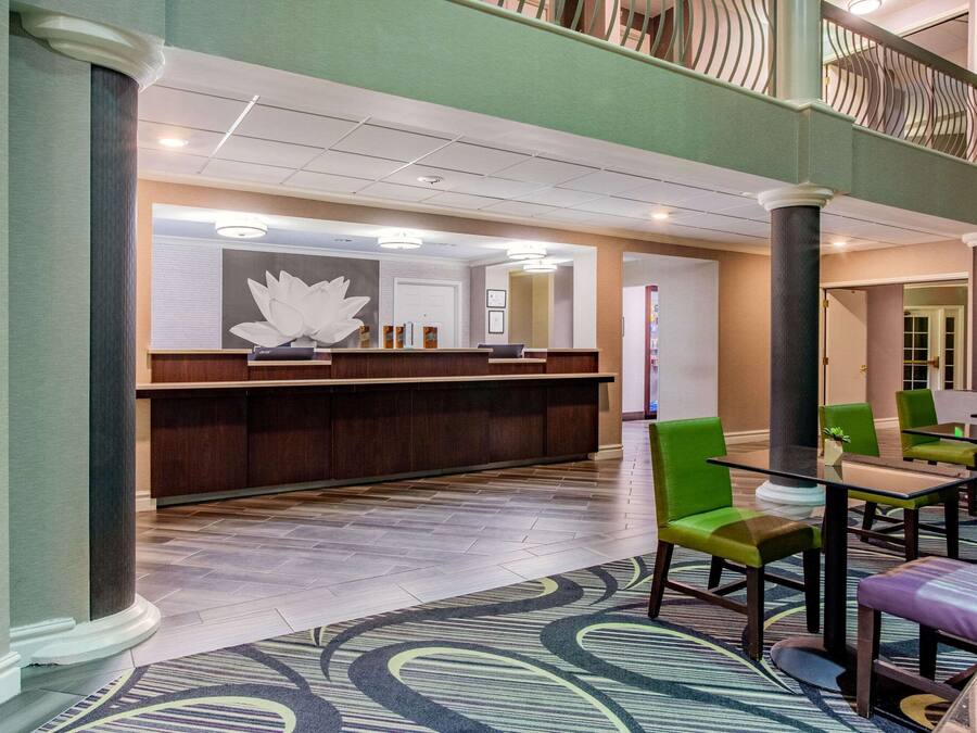 Um saguão de hotel com balcão de recepção, cadeiras verdes e um tapete estampado.
