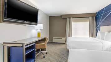Quarto de hotel com televisão de tela plana, uma escrivaninha com cadeira, duas camas, uma janela com cortinas e ar condicionado.