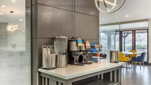 Cozinha moderna com eletrodomésticos de aço inoxidável, máquina de café e um espaço de estar com cadeiras amarelas e azuis.