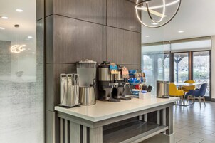 Cozinha moderna com eletrodomésticos de aço inoxidável, máquina de café e um espaço de estar com cadeiras amarelas e azuis.