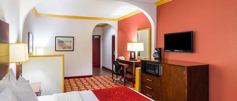 Quarto de hotel com cama, escrivaninha e televisão.