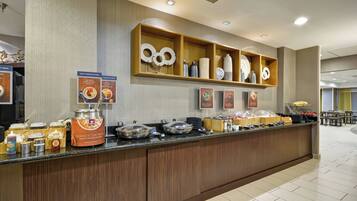 Um balcão de buffet de café da manhã com diversos alimentos e recipientes, incluindo um grande recipiente de Quaker Aveia.