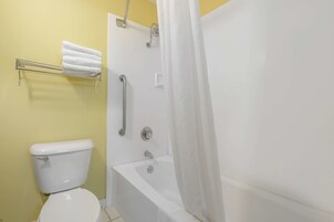 Um banheiro com vaso sanitário branco, banheira com cortina de chuveiro e porta-toalhas com toalhas dobradas.