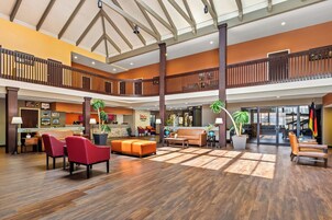 Um hall amplo com teto alto, piso de madeira e área de estar central com sofás vermelhos e laranja.