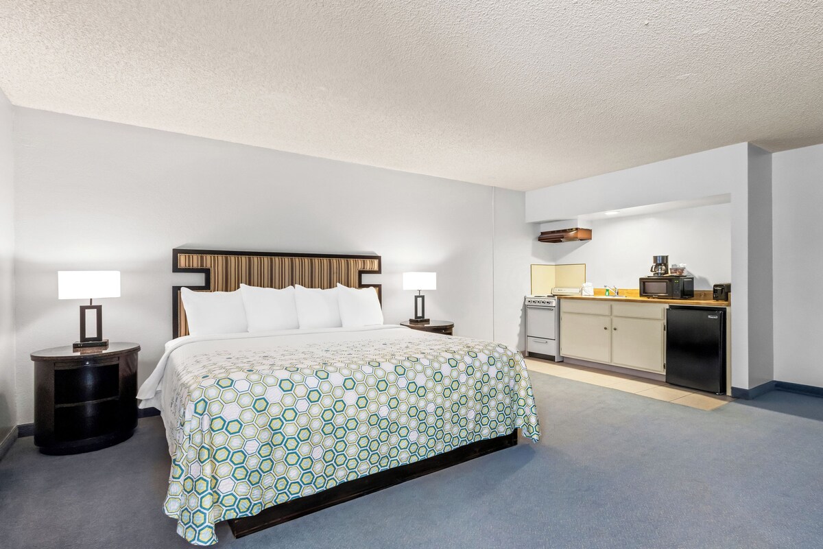 Quarto de hotel com cama, mesas de cabeceira, pequeno espaço de cozinha e banheiro.