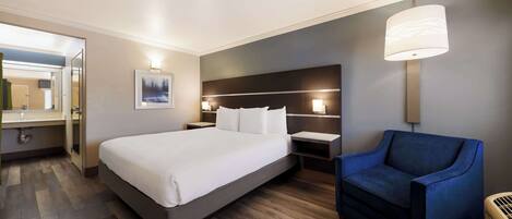 Quarto de hotel com uma cama grande, mesas de cabeceira, uma cadeira, um abajur e um espelho.