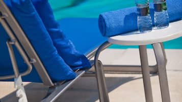 Uma área de estar à beira da piscina com uma cadeira azul, uma mesa redonda pequena e duas garrafas de água.