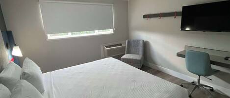 Quarto de hotel com uma cama grande, uma cadeira, uma escrivaninha, televisão de tela plana e uma janela.