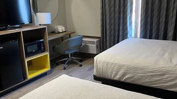 Quarto de hotel com uma cama, uma escrivaninha com cadeira, televisão, espelho e janela com cortinas.