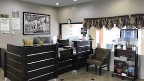 Uma área de recepção com uma mesa preta, um computador, um relógio e uma janela com cortinas.