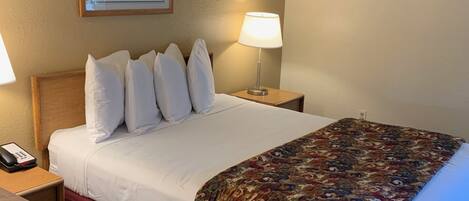 Quarto de hotel com cama, mesa de cabeceira com abajur, telefone e um quadro na parede.