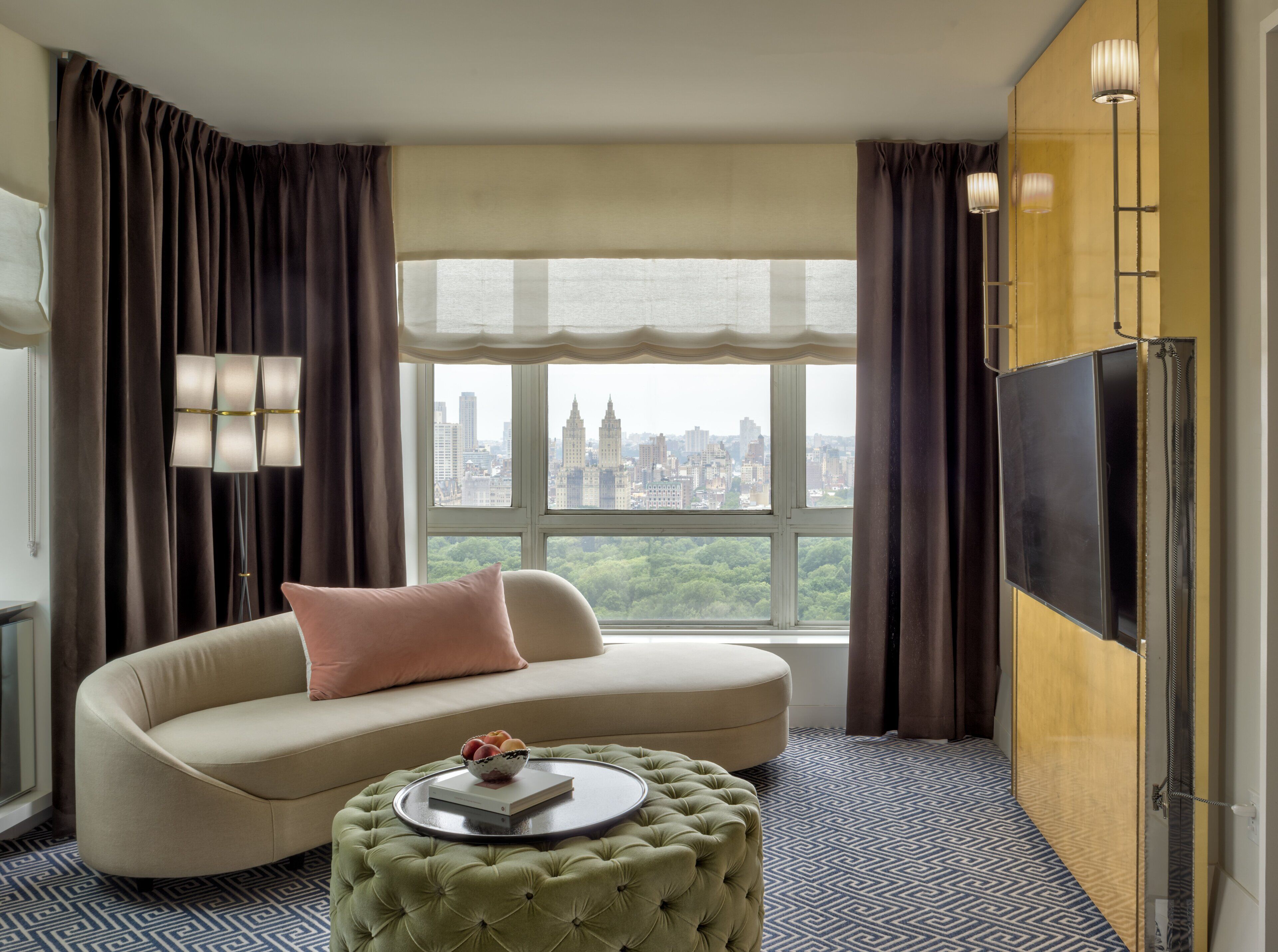 Quarto de hotel com sofá, apoio para os pés e televisão de tela plana.