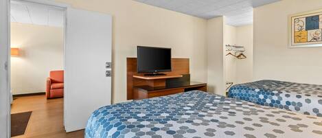 Quarto de hotel com duas camas, televisão, escrivaninha e porta que dá para outro cômodo.