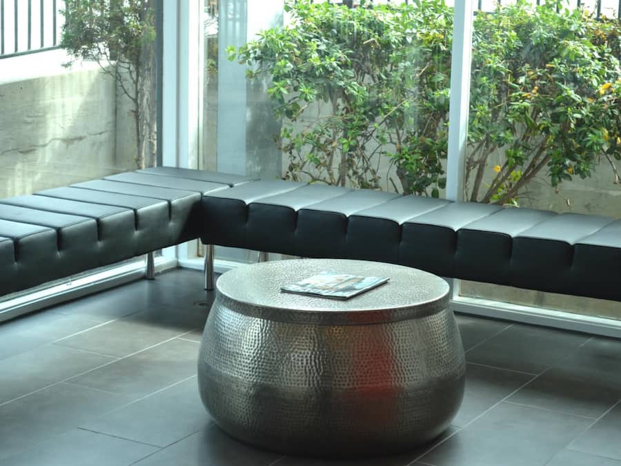 Uma área de estar moderna com um banco e uma mesa redonda, uma parede de concreto e vista para o verde lá fora.