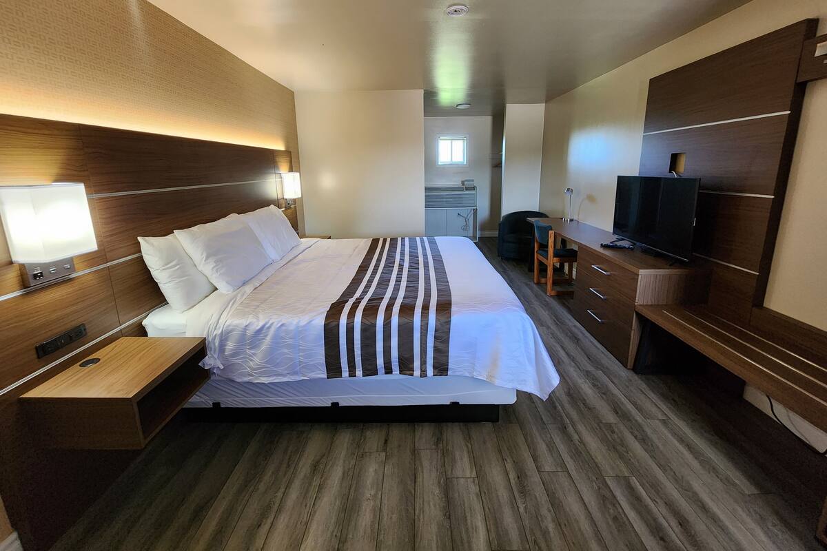 Quarto de hotel com uma cama grande, mesas de cabeceira, uma escrivaninha com cadeira, televisão e guarda-roupa.