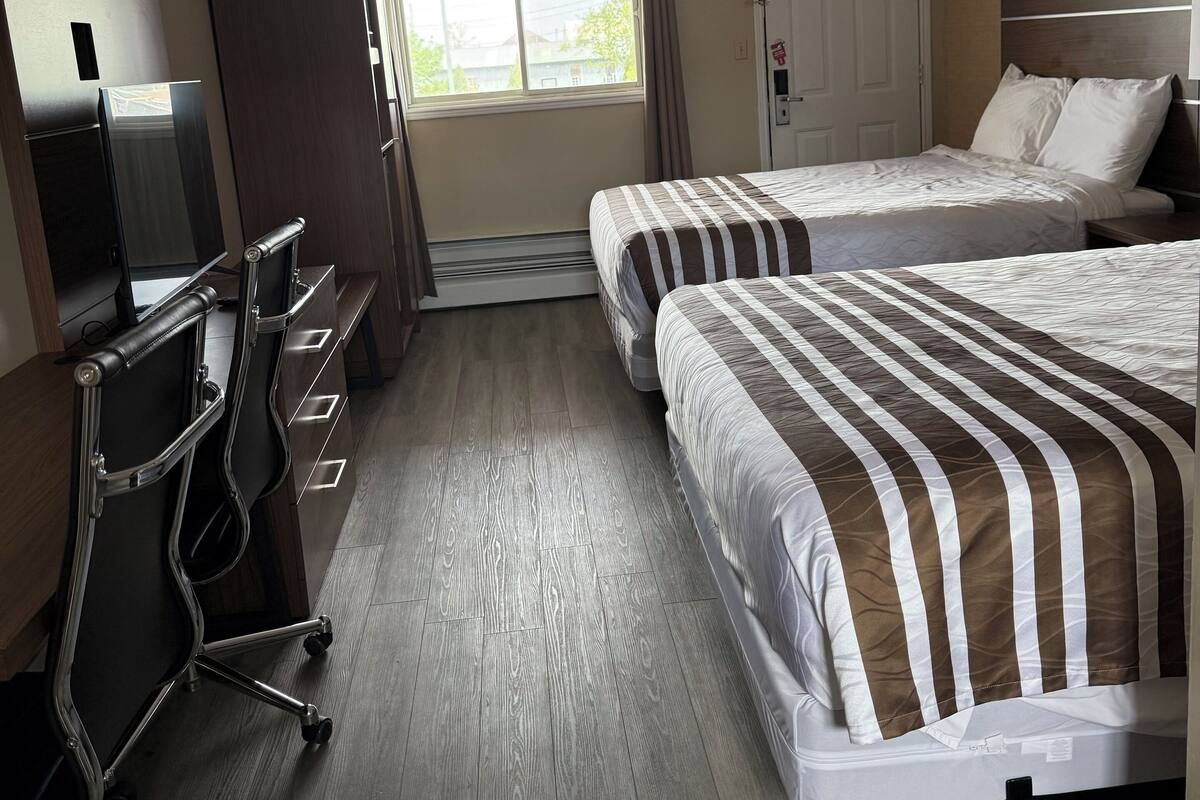 Quarto de hotel com duas camas, uma escrivaninha, uma cadeira e uma janela.