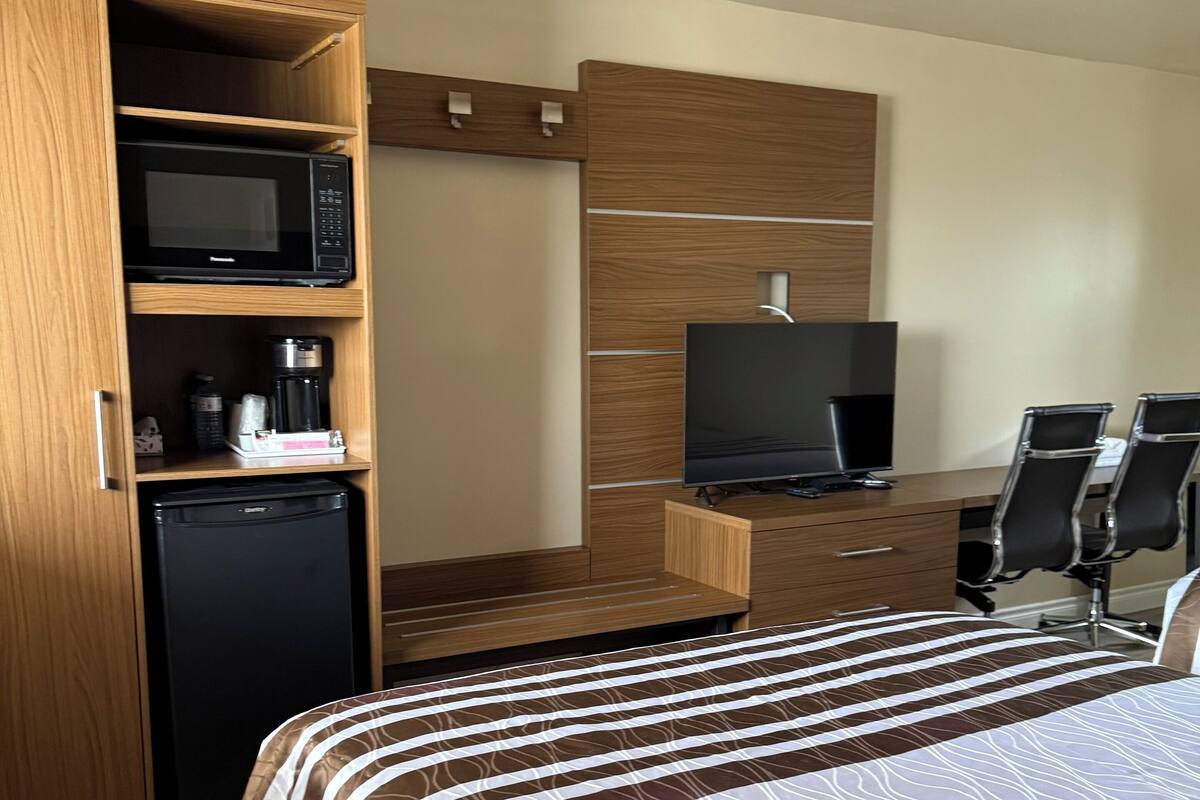 Quarto de hotel com cama, escrivaninha, televisão, micro-ondas e frigorífico.