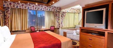 Quarto de hotel com cama, televisão, escrivaninha e banheiro com banheira.