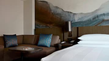 Quarto de hotel com cama, sofá, mesa de cabeceira e um quadro na parede.