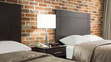 Quarto de hotel com parede de tijolos, uma cama com roupa de cama branca, mesa de cabeceira com abajur e um telefone.