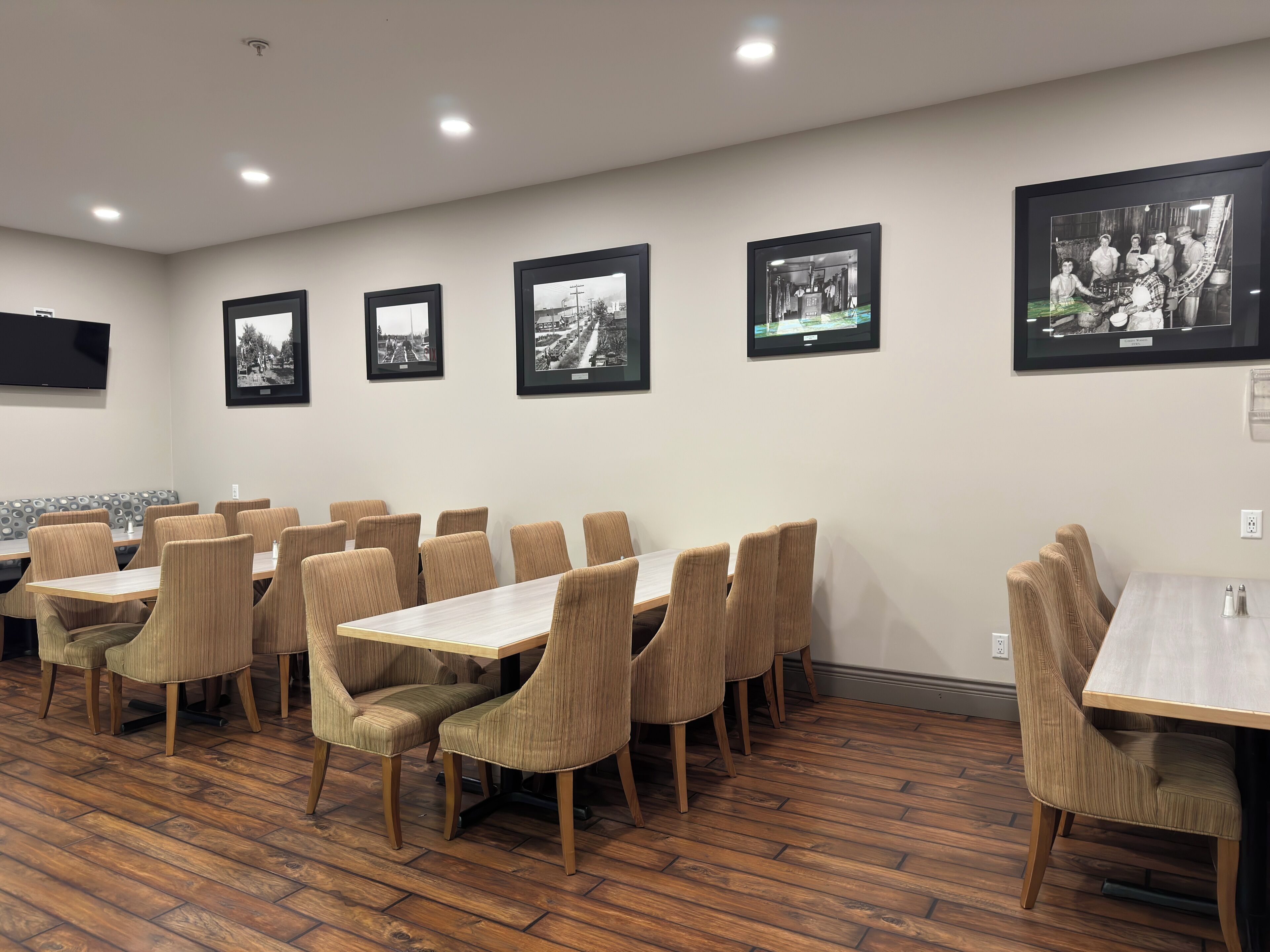 Uma sala de conferências com várias mesas e cadeiras, uma televisão de tela plana na parede e fotografias em preto e branco emolduradas.