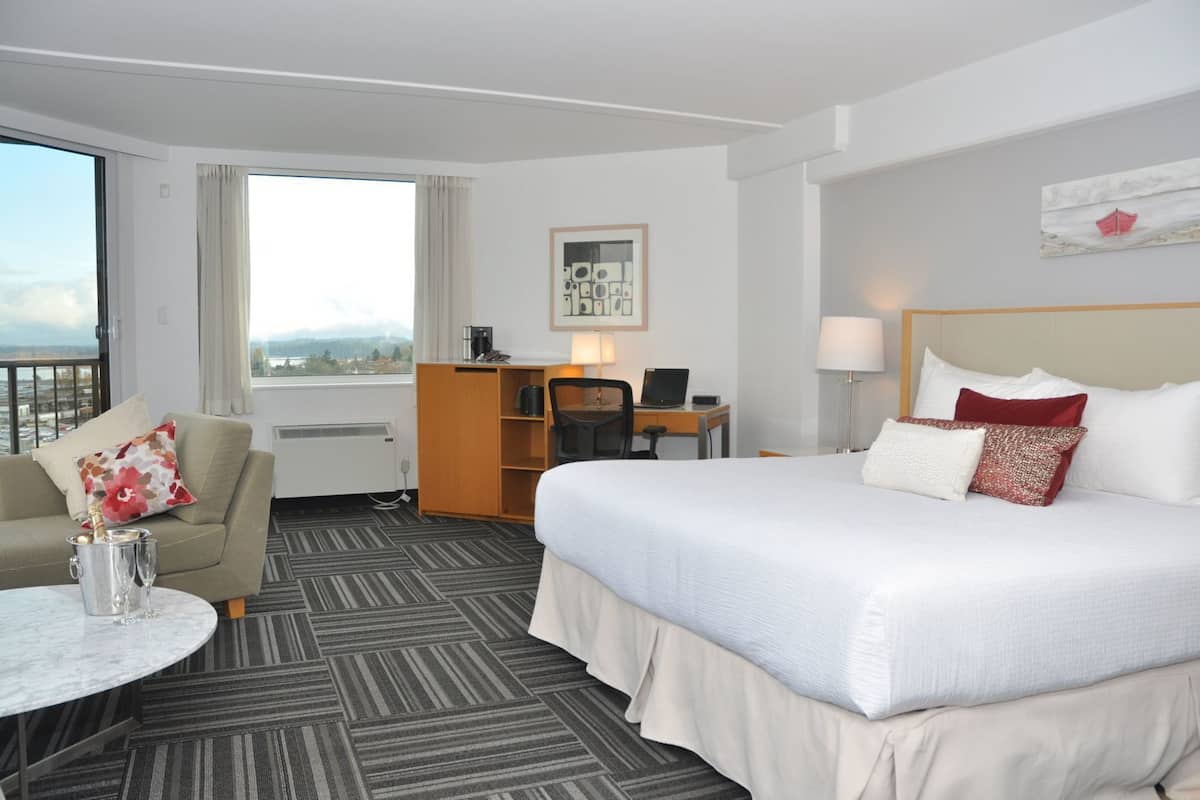 Quarto de hotel com cama, escrivaninha, cadeira, mesinha e vista para o exterior.
