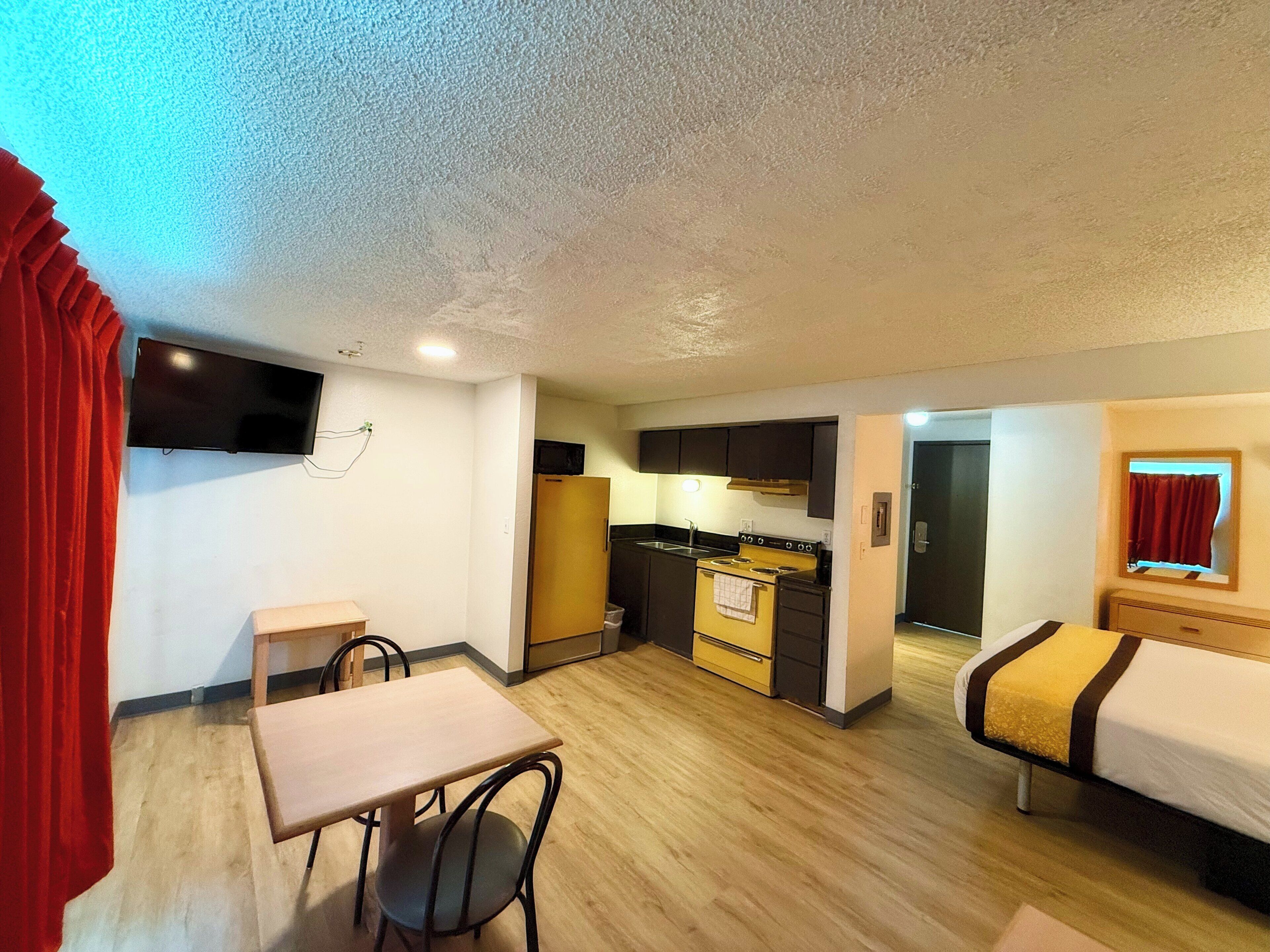 Quarto de hotel com mesa de jantar, duas camas, cozinha compacta e televisão.