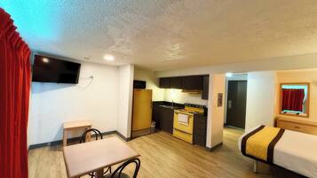 Quarto de hotel com mesa de jantar, duas camas, cozinha compacta e televisão.