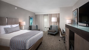 Quarto de hotel com uma cama grande, duas poltronas, uma escrivaninha com televisão e uma mesa pequena com luminárias.