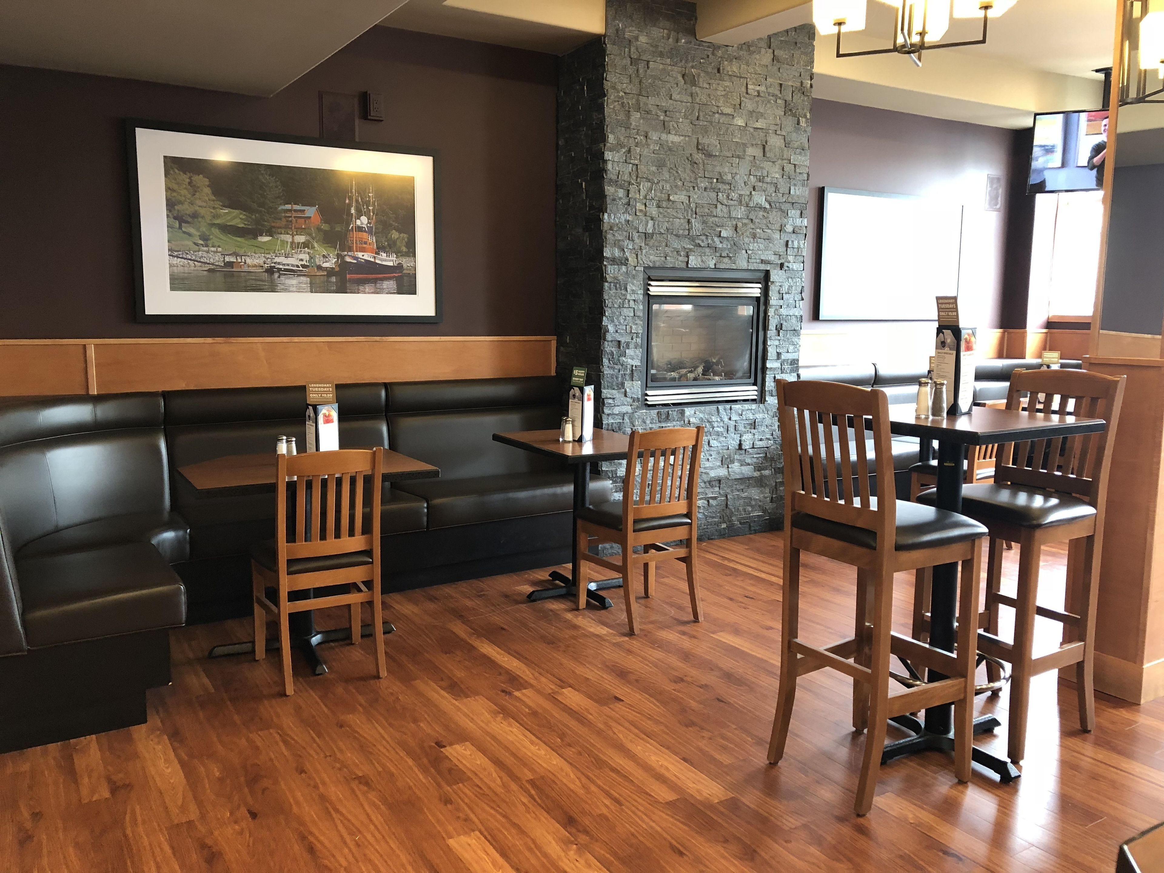 Um restaurante com mesas e cadeiras de madeira, um assento de couro preto e uma parede de pedra com lareira.