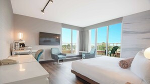 Quarto de hotel com cama, escrivaninha, cadeira, televisão e varanda com vista.