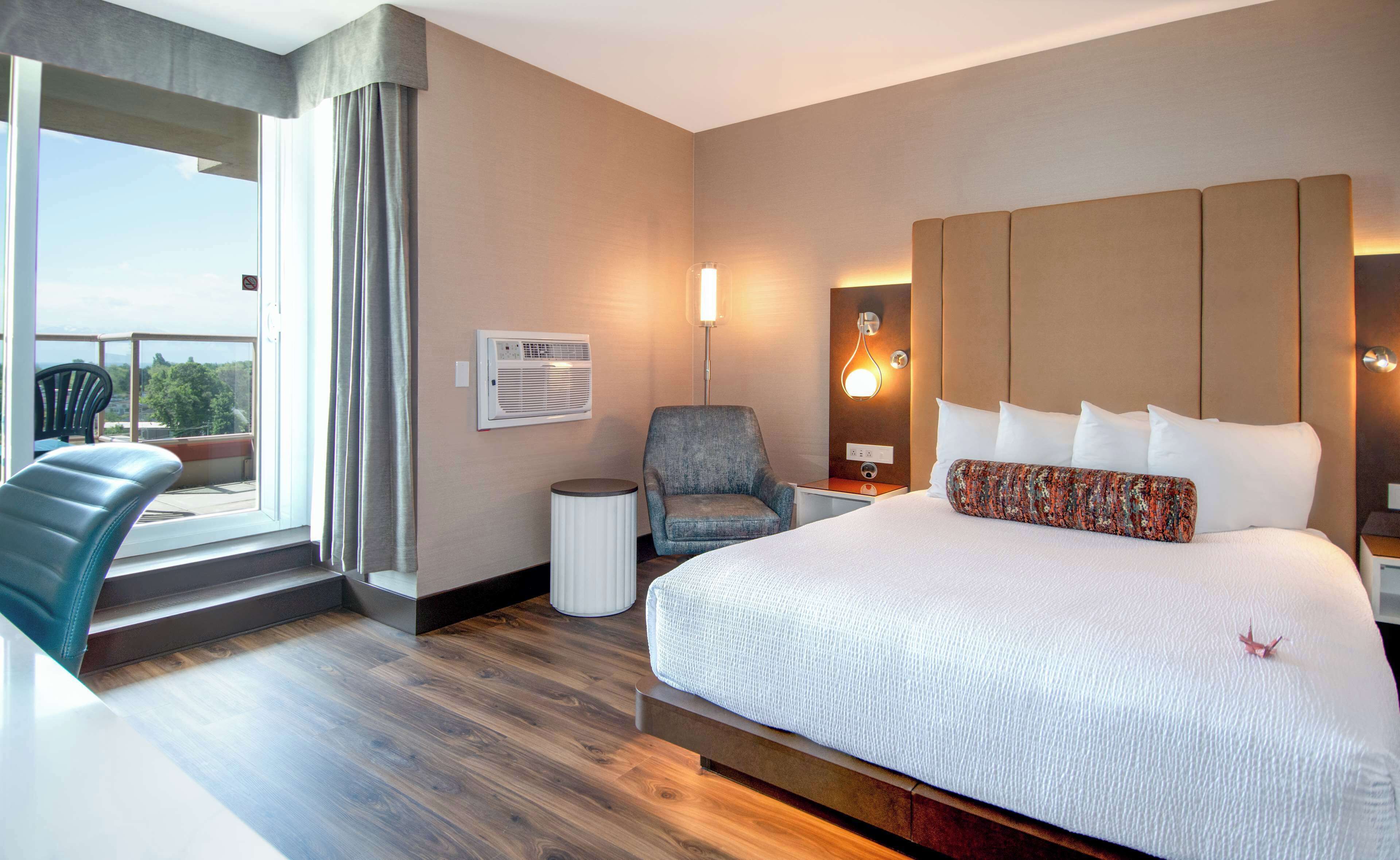 Quarto de hotel com uma cama grande, uma cadeira, uma escrivaninha e vista para o exterior.