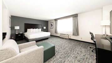 Quarto de hotel com cama, escrivaninha, cadeira e uma janela grande com cortinas.
