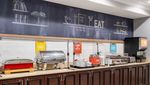 Um balcão de café da manhã com diversas estações de comida, incluindo um aviso para ovos, uma máquina de café e uma seção de padaria.