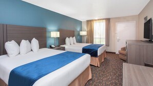 Quarto de hotel com duas camas, uma escrivaninha, uma televisão e uma porta.