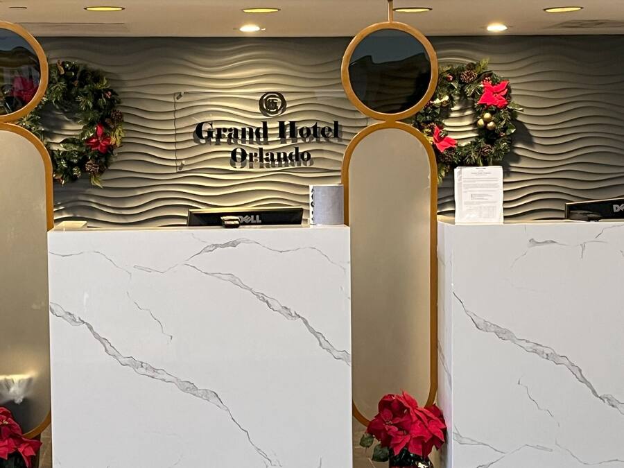 Bancada de recepção do Grand Hotel Orlando com design em mármore, dois espelhos redondos e guirlandas decorativas.