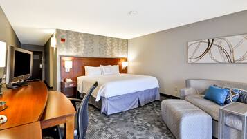 Quarto de hotel com cama, sofá, escrivaninha e televisão.