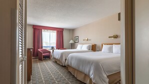Quarto de hotel com duas camas, uma escrivaninha, uma cadeira e uma janela com cortinas.