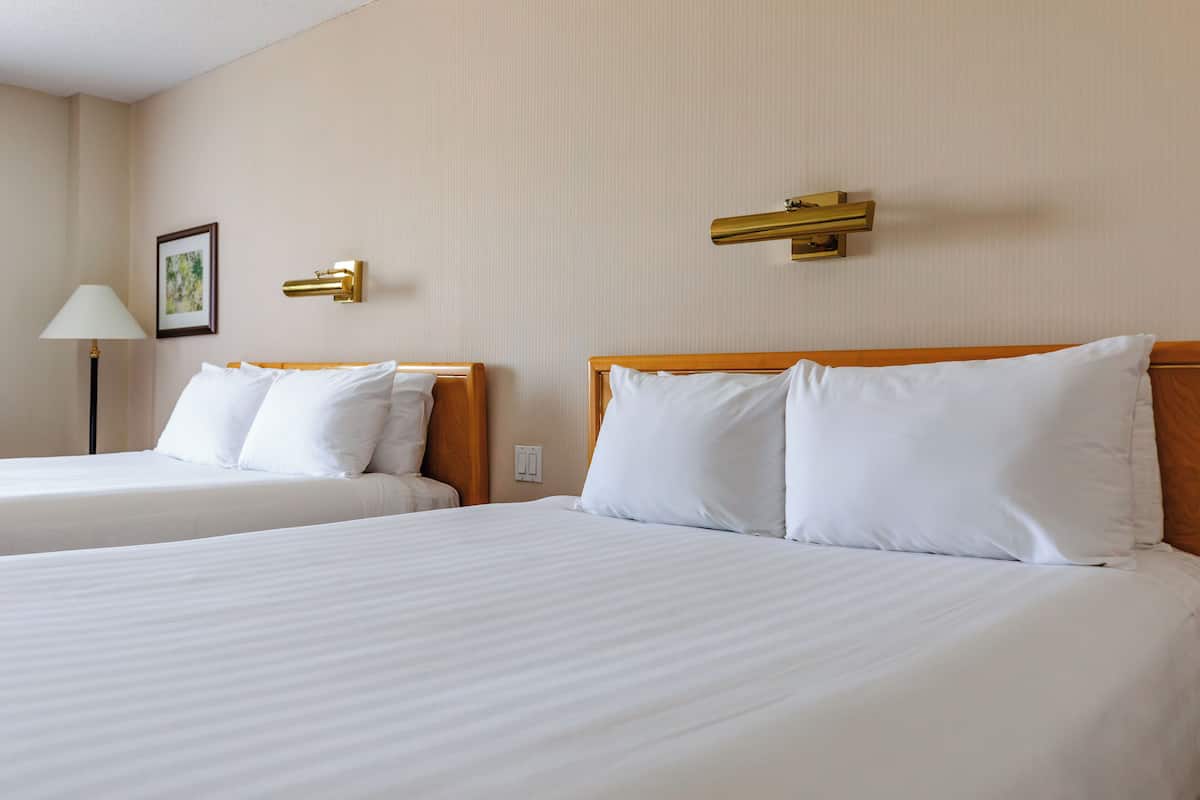 Quarto de hotel com duas camas, uma lâmpada e luminárias fixadas na parede.