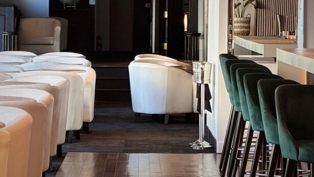Um lobby moderno de hotel com balcão de recepção, área de estar com cadeiras e escadaria para outro nível.